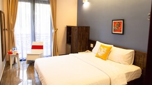 Quarto de hotel com cama, escrivaninha, cadeira, guarda-roupa e janela com cortinas.