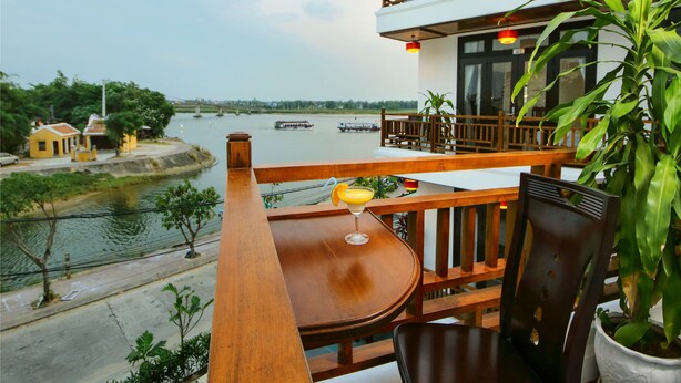 Uma varanda com vista para um rio e barcos, uma mesa com bebida e um vaso de planta.