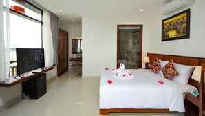 Quarto de hotel com uma cama grande, televisão, uma pequena escrivaninha e um quadro na parede.