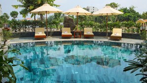Área de piscina com espreguiçadeiras e guarda-sóis, cercada por vegetação e um muro de pedra.