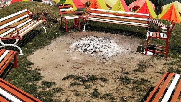 Um camping com tendas coloridas, bancos de madeira e uma placa com a inscrição 'The Sky Village'.