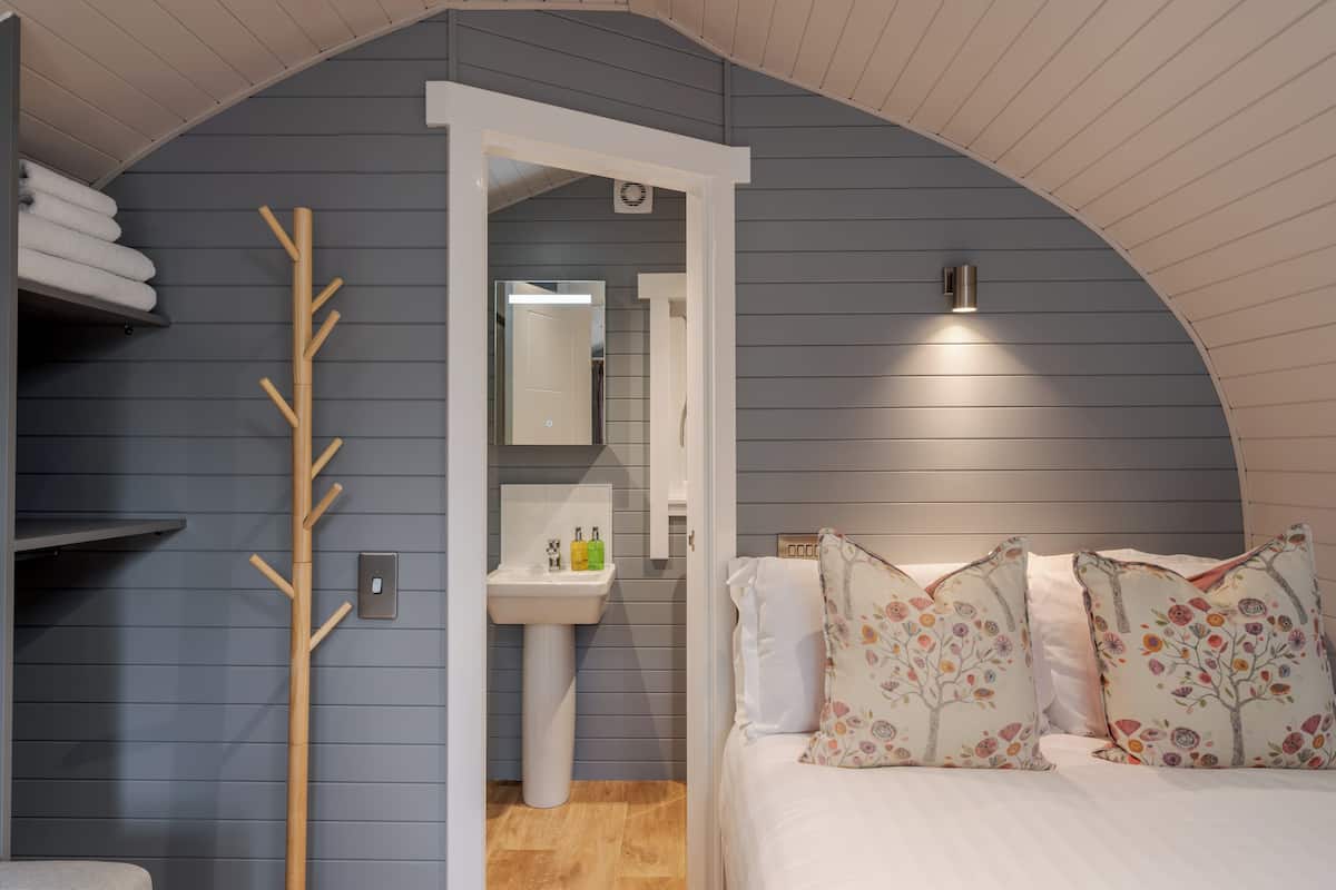 Quarto com teto curvo, porta-roupas de madeira, piaça branca e almofadas florais.