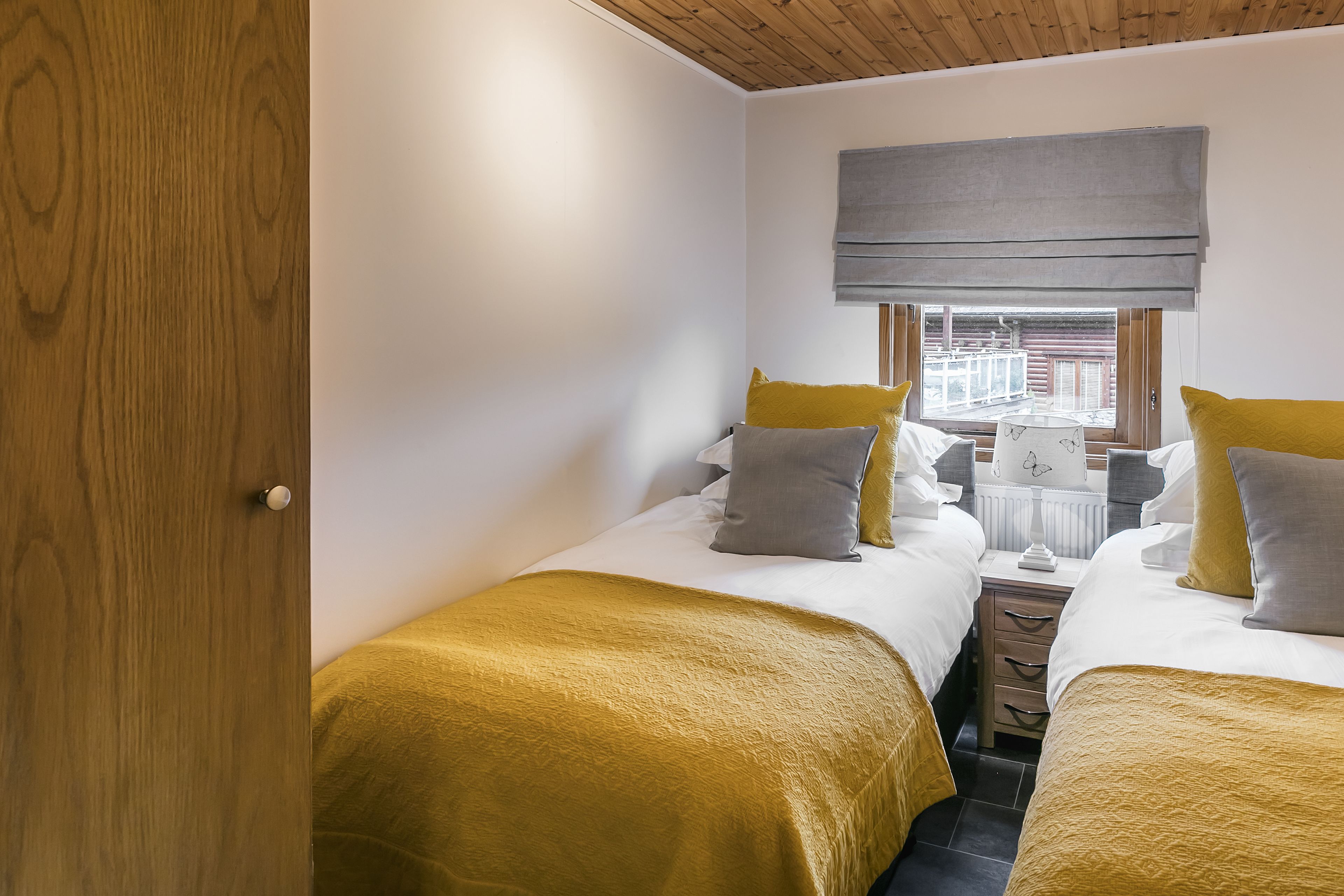 Quarto com duas camas, porta de madeira, janela com vista e cortina cinza.