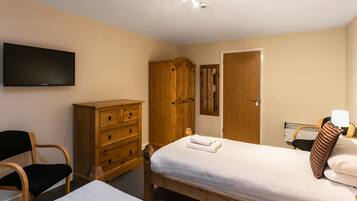 Quarto com cama, cómoda de madeira, televisão e porta.