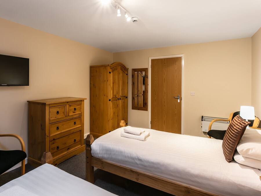 Quarto com cama, cómoda de madeira, televisão e porta.