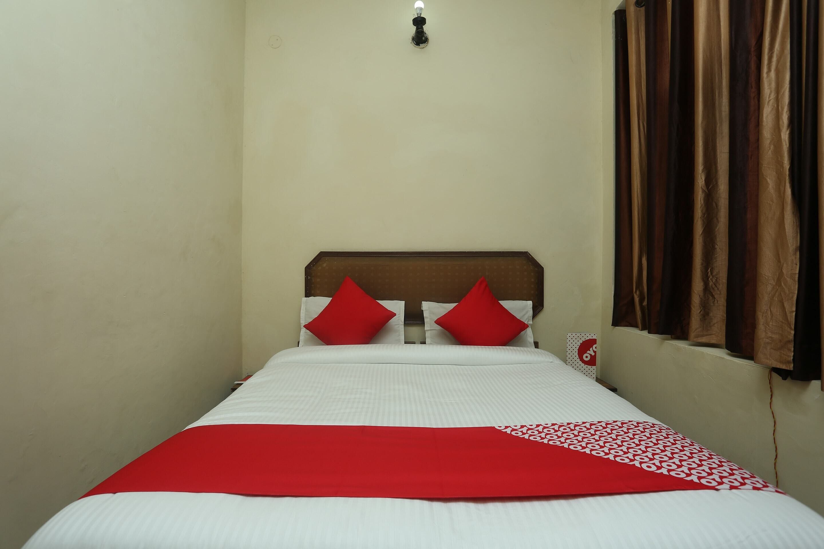 Uma cama de solteiro com cabeceira de madeira, duas almofadas vermelhas e um edredom branco e vermelho.
