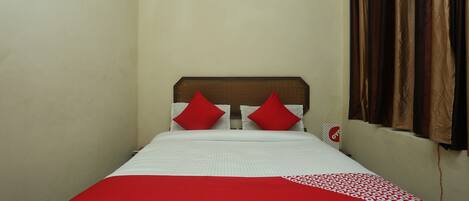 Uma cama de solteiro com cabeceira de madeira, duas almofadas vermelhas e um edredom branco e vermelho.