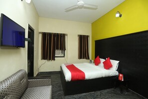 Quarto de hotel com cama, televisão, ventoinha no teto e janela com cortinas.