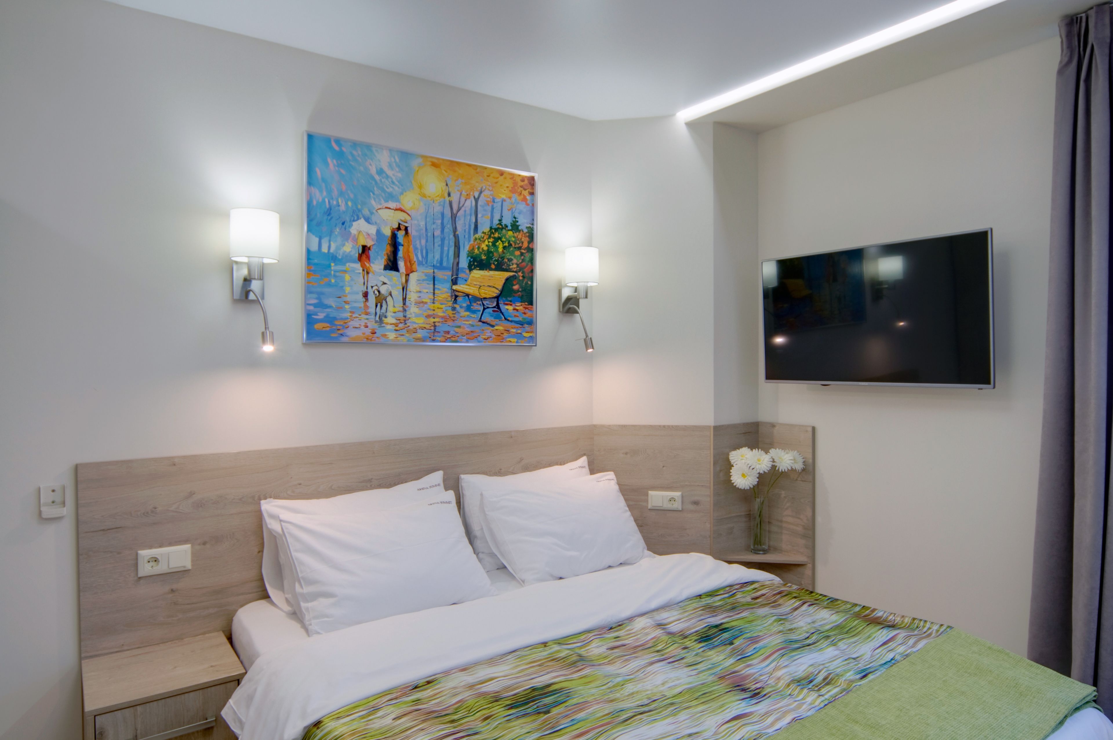 Quarto de hotel com cama, um quadro, televisão e mesa de cabeceira com abajur.