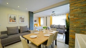 Sala de estar moderna com área de jantar, apresentando um conjunto de sofá, mesa de jantar com cadeiras e uma janela grande que proporciona iluminação natural.