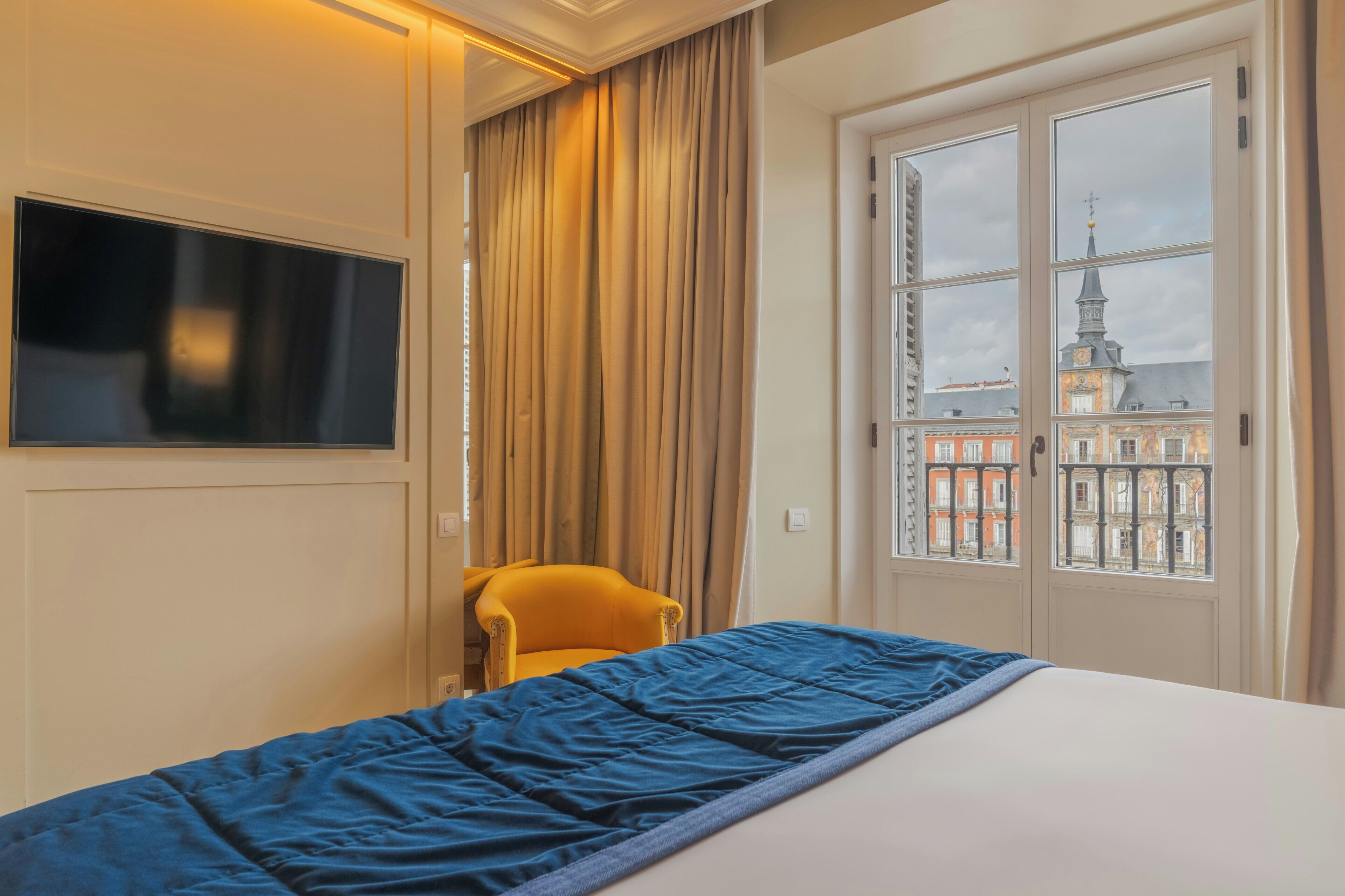 Quarto de hotel com cama, uma cadeira, televisão e janela com vista para um edifício.