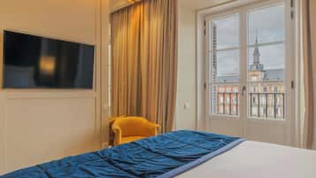 Quarto de hotel com cama, uma cadeira, televisão e janela com vista para um edifício.