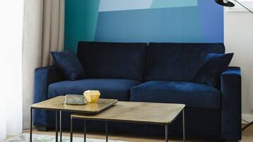Uma sala de estar moderna com um sofá azul, uma mesa de centro de madeira e um mural geométrico na parede.