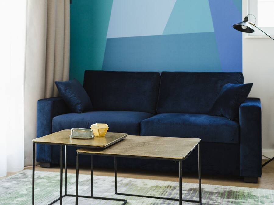 Uma sala de estar moderna com um sofá azul, uma mesa de centro de madeira e um mural geométrico na parede.