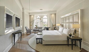 Quarto de hotel com uma cama grande, escrivaninha, cadeira, televisão e janela com cortinas.