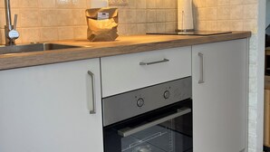 Uma cozinha moderna com armários brancos, uma pia de aço inoxidável, forno embutido e bancada com dispensador de papel toalha.