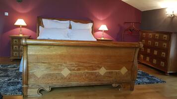 Uma cama de madeira com cabeceira, duas luminárias de apoio, um penteado e um tapete estampado em um quarto com paredes roxas.