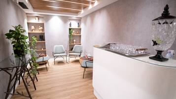 Uma área de recepção moderna com um balcão de madeira, espaço de estar com cadeiras e prateleiras com objetos decorativos.