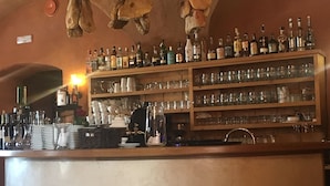 Uma área de bar com prateleiras de garrafas de bebidas, copos e carnes penduradas.