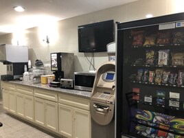 Uma cozinha equipada com máquina de café, micro-ondas, torradeira, geladeira com lanches e um distribuidor automático.