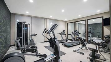 Uma academia com diversos aparelhos de exercícios, incluindo esteiras e elípticos, e um espelho grande na parede.