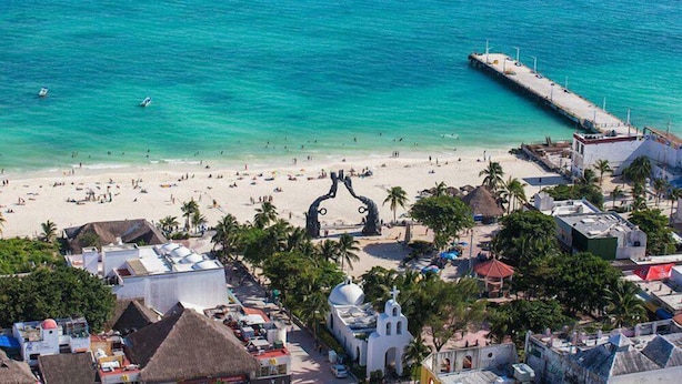 Uma praia com um píer, uma igreja e uma estátua.