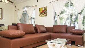 Um sofá de couro marrom com almofadas, uma mesa de centro de vidro e um quadro na parede.