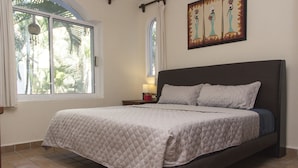 Quarto com cama, janela, mesa de cabeceira, abajur e quadro na parede.
