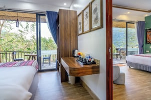 Quarto de hotel com cama, escrivaninha com cafeteira e varanda com vista para o verde.