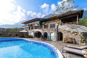 Hotel com piscina, fachada de pedra e vista para as montanhas.