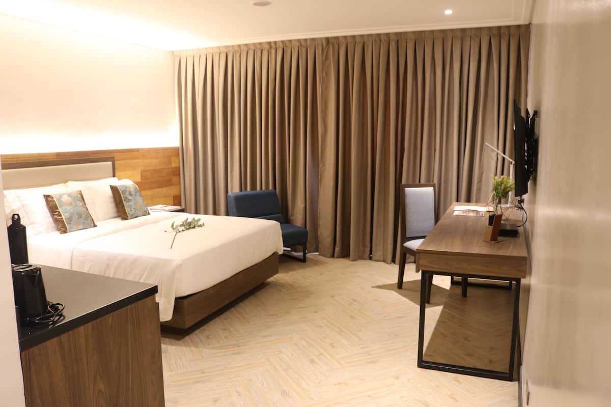 Quarto de hotel com cama, escrivaninha, cadeira e televisão.