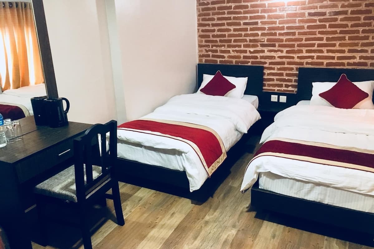 Quarto de hotel com duas camas, uma escrivaninha, uma cadeira e uma parede de tijolos.