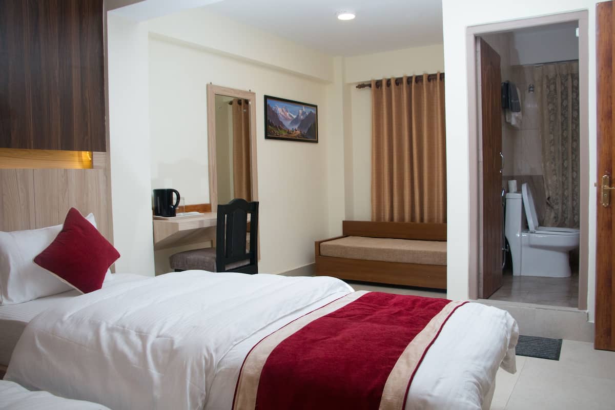 Quarto de hotel com cama, escrivaninha, cadeira, banheiro e chuveiro.