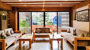 Uma sala de estar acolhedora com vigas de madeira, um conjunto de sofá, uma mesa de centro e vista para um jardim através de grandes portas deslizantes.