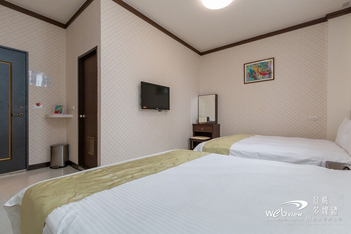 Quarto de hotel com duas camas, televisão, espelho e uma pequena prateleira com objetos.