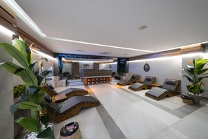 Uma área de spa moderna com várias poltronas de descanso, um balcão de recepção e plantas decorativas.