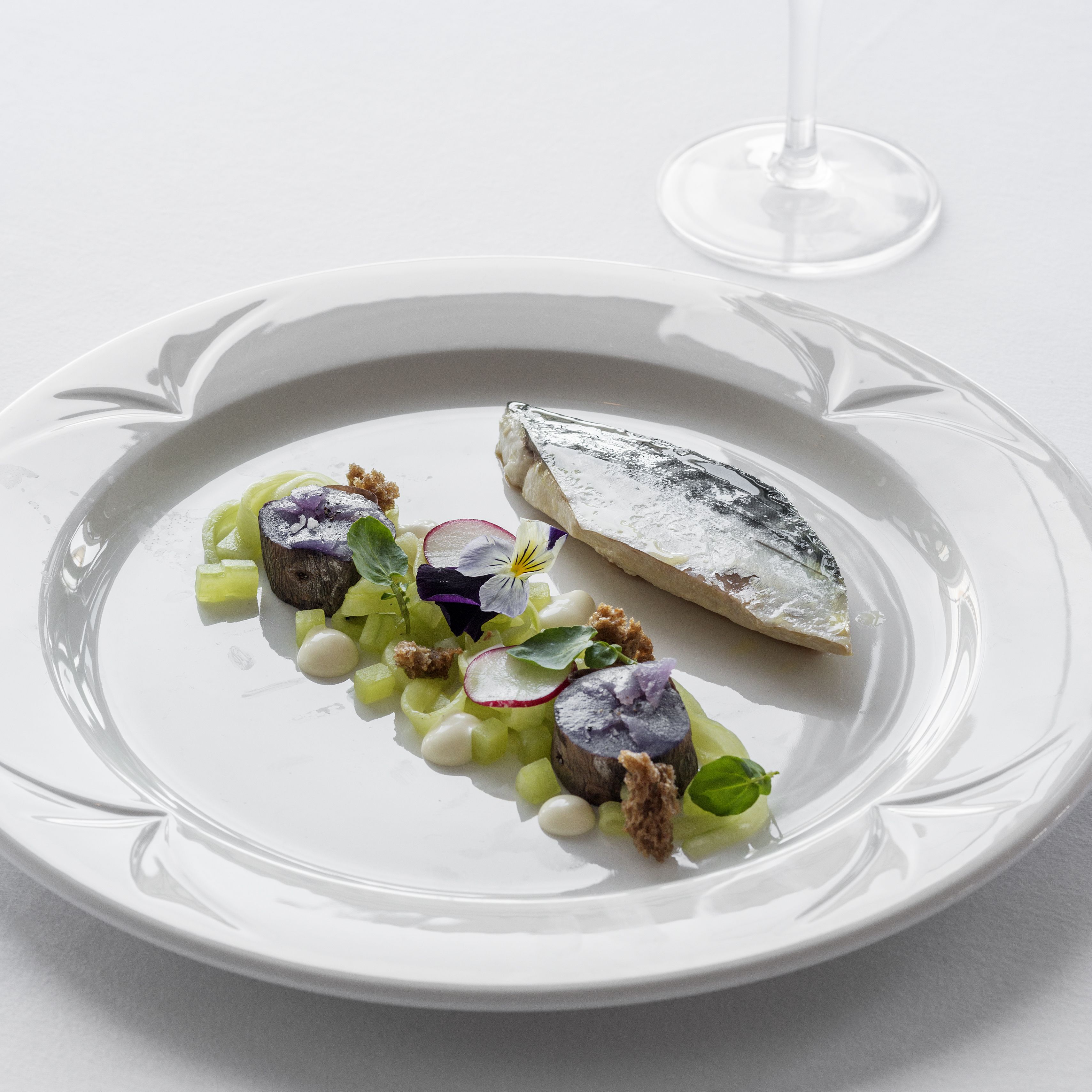 Um prato branco com peixe, vegetais verdes e uma taça de vinho.