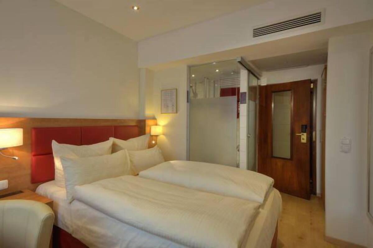 Quarto de hotel com uma cama grande, duas mesas de cabeceira, uma cadeira e um espelho.