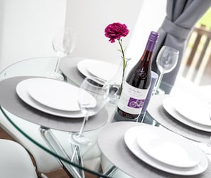 Uma mesa posta com pratos brancos, uma garrafa de vinho e um vaso de vidro com uma flor rosa.