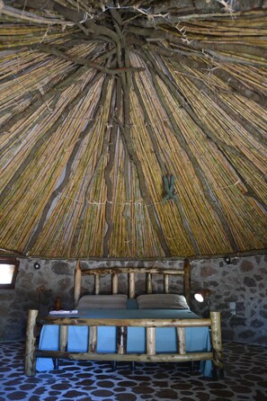 Um quarto rústico com telhado de palha, cama de madeira e parede de pedra.