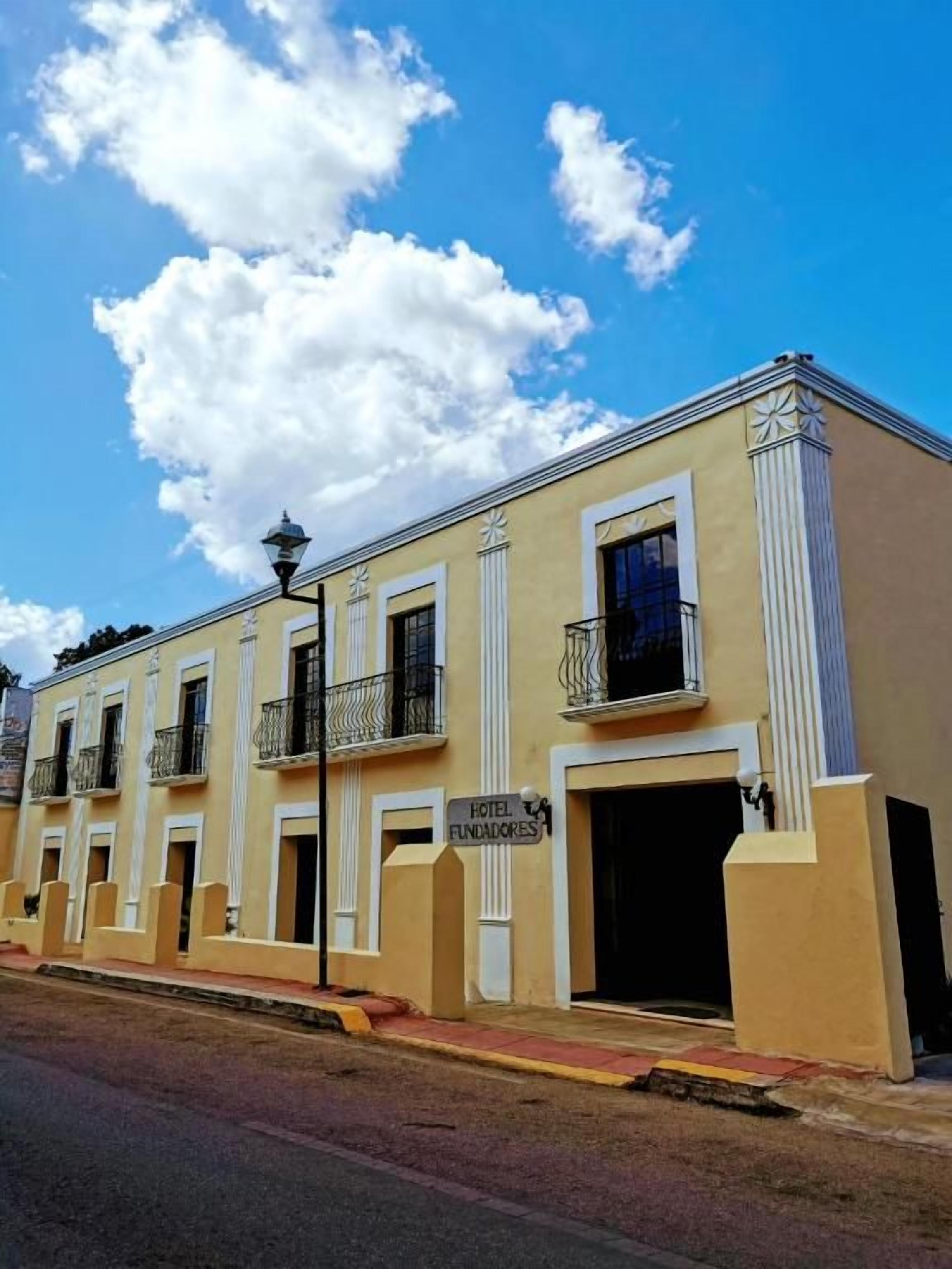 Um hotel com fachada amarela, várias varandas e uma placa indicando que é um hotel.