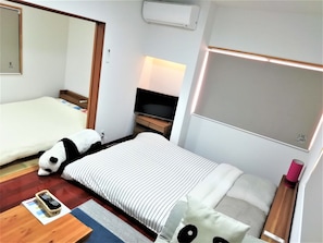 Quarto de hotel com cama, televisão, mesa de cabeceira e ar condicionado fixado na parede.