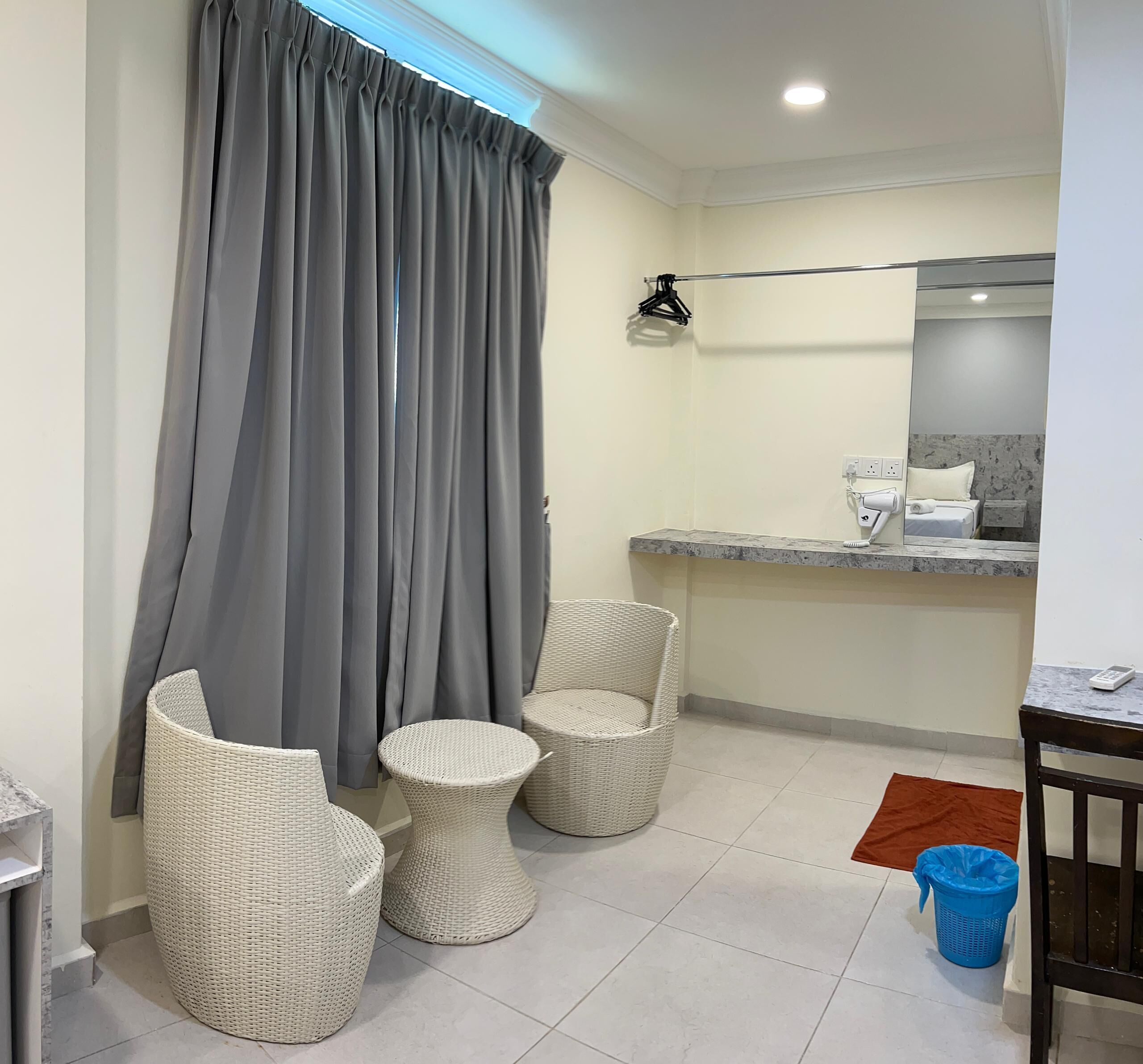 Casa de banho com cortinas cinzentas, espelho, secador de cabelo e mobiliário de vime.