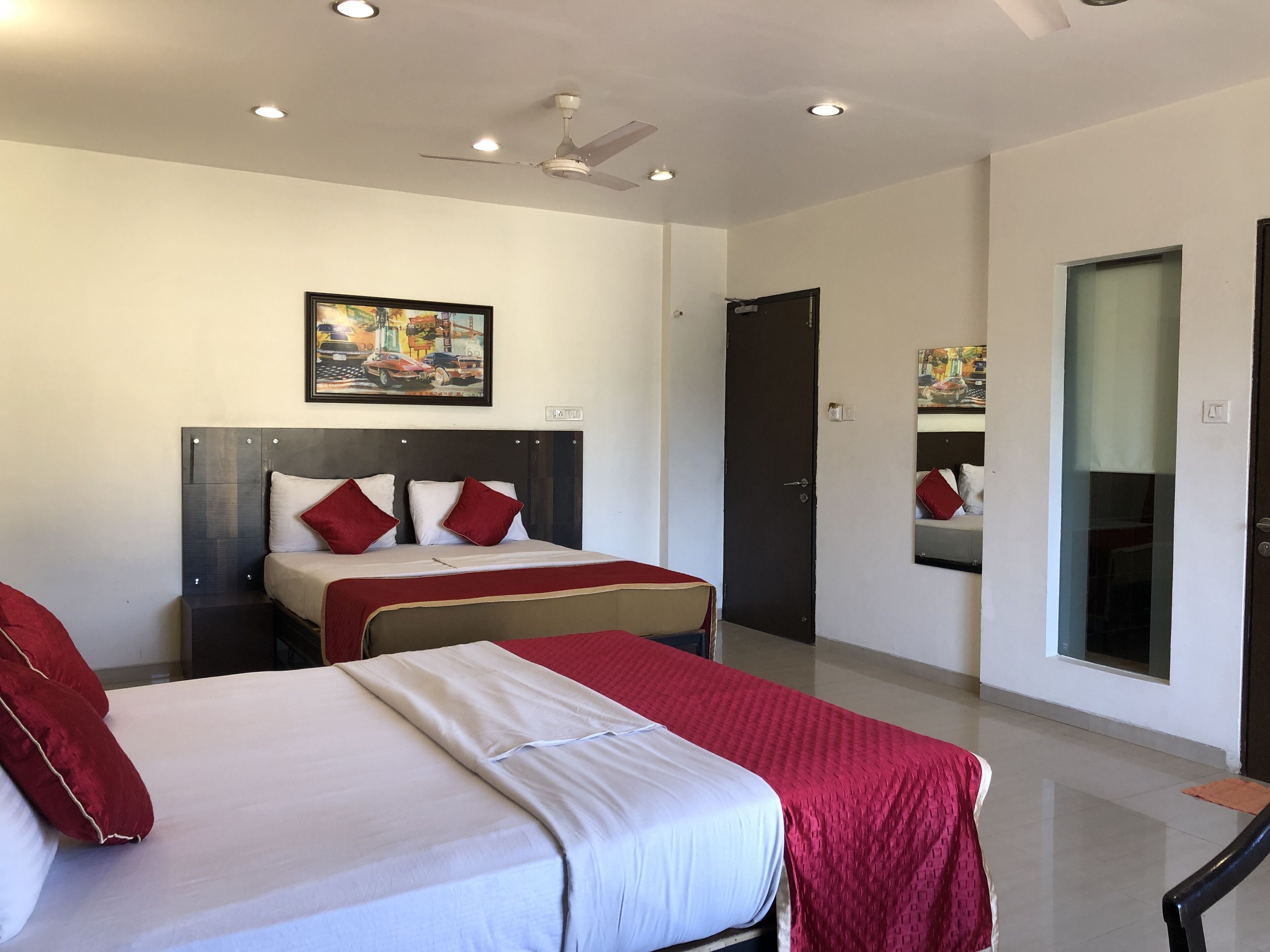 Quarto de hotel com duas camas, ventilador de teto, iluminação embutida e obras de arte nas paredes.