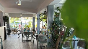 Ampla área de refeições interna com piso de madeira e móveis modernos, com grandes janelas e plantas dentro de casa.