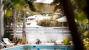 Uma área de piscina com cadeiras de sol brancas, cerca branca e palmeiras.