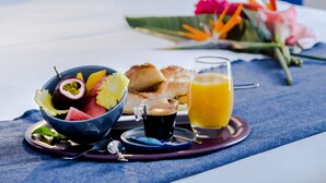 Café da manhã montado em uma cama de hotel, com uma tigela de frutas, um copo de suco de laranja e uma xícara de café.