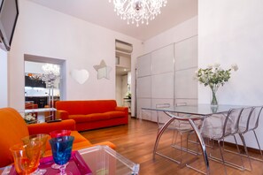 Uma sala de estar moderna com uma mesa de jantar de vidro, sofá laranja e peças de vidro coloridas.