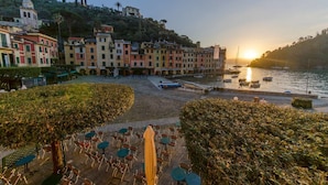 Uma vila costeira com edifícios coloridos, um porto de iates e vista para o pôr do sol.