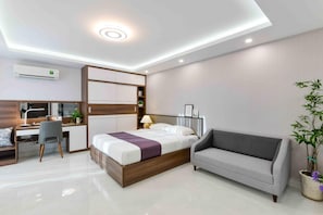 Quarto de hotel moderno com uma cama, uma escrivaninha, um sofá e um vaso de planta.